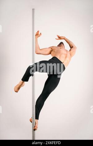 Muscular man is gracefully holding a pole dance pose, showcasing ...