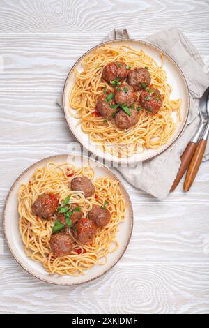 Two plates of delicious spaghetti with meatballs served on white wooden ...