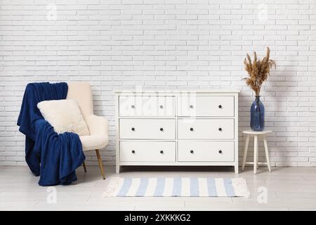 Chest of drawers with decor, coffee table and pouf near white brick ...