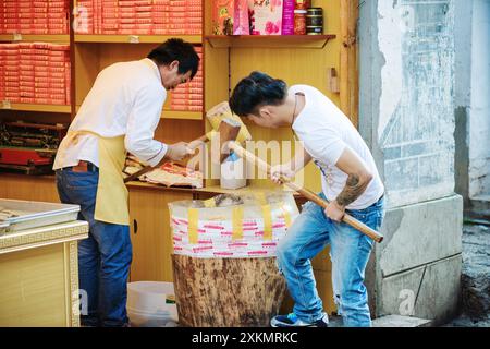 Chinese men with wooden mallets are crushing nuts to make sweets Stock ...