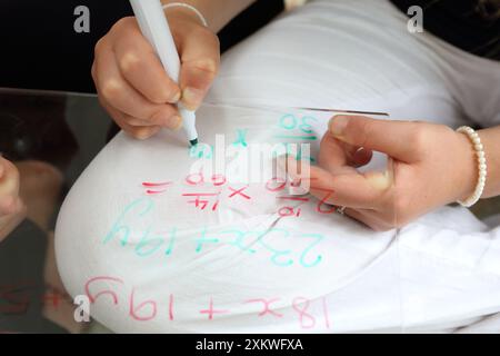 Girls doing maths math sitting on floor writing on whiteboard with pens ...