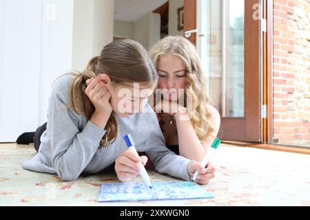 Two girls doing maths math lying on floor writing on whiteboard with ...