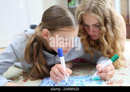 Girls doing maths math lying on floor writing on whiteboard with pens ...