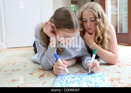 Girls doing maths math lying on floor writing on whiteboard with pens ...
