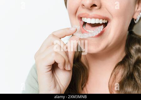 A smiling woman inserts a clear teeth aligner, straightening teeth ...