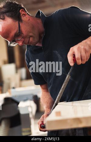 Carpenter wearing safety glasses is smoothing a wood plank in his ...