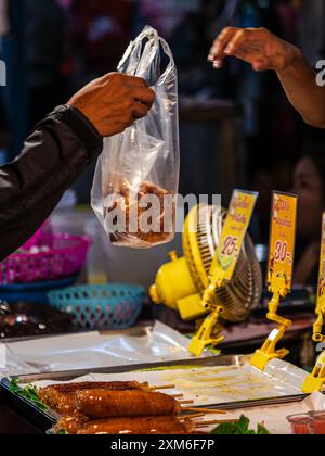 Street food vendor grilling skewered sausages and burgers at a market ...