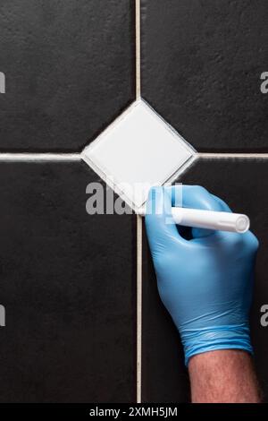Person wearing gloves using grout pen on floor tiles to restore white ...