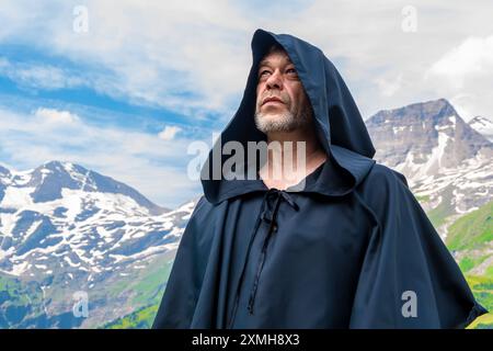 Mysterious elderly male monk wearing a hooded cloak, standing amidst ...