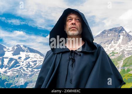 Mysterious elderly male monk wearing a hooded cloak, standing amidst ...