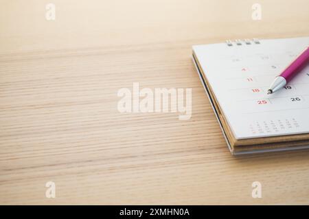 calendar page with pen point at 25th date on wood table background ...