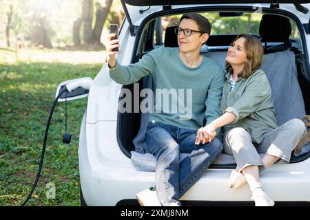Loving couple with smartphones sits in an electric car's trunk Stock ...