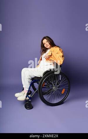 A young woman in a wheelchair poses in a studio with a purple ...