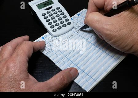Man making entry in check register with calculator Stock Photo - Alamy