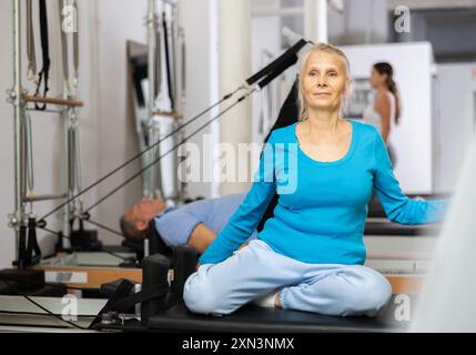 Senior female performing mermaid exercise on reformer Pilates machine ...