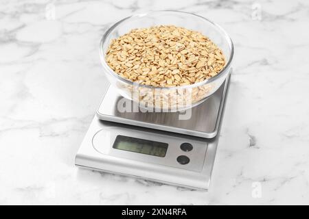 Kitchen scale with bowl of dry oats on white marble table, top view ...