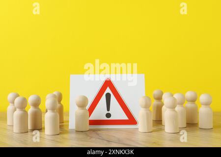 Wooden human figures among warning road sign on table against yellow ...