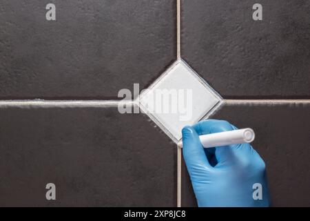 Person wearing gloves using grout pen on floor tiles to restore white ...