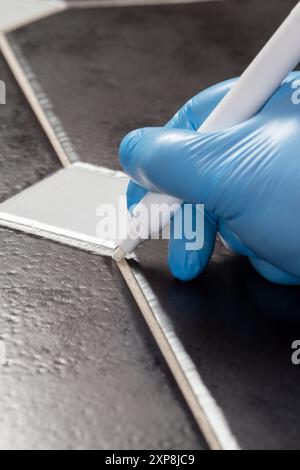 Person wearing gloves using grout pen on floor tiles to restore white ...