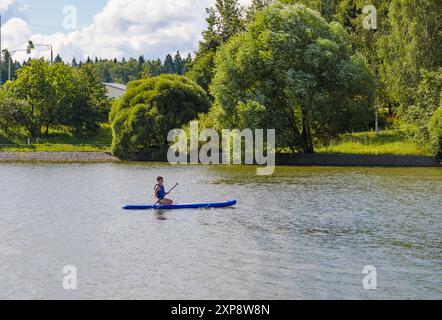 A young guy sitting down rides a SUP board, overcoming the waves with ...
