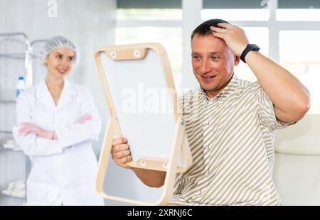 Nurse holds a mirror, satisfied man examines his face in mirror after ...