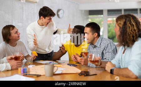 Group of enthusiastic men playing board game sitting around table Stock ...