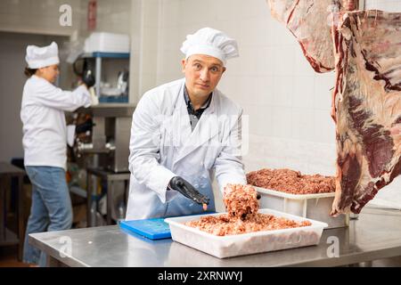 Positive male butcher making ground beef in butcher shop Stock Photo ...