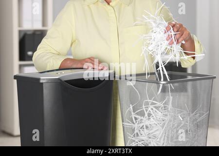 Woman putting shredded paper strips into trash bin at white table in ...