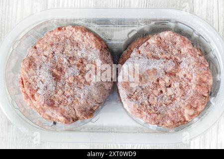 Frozen beef burgers in plastic tray packaging thawing. On a grey wood ...