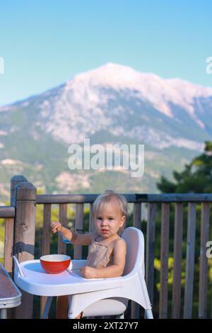 Adorable toddler eating porridge sitting on highchair at home Stock ...