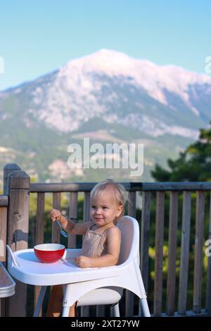 Adorable toddler eating porridge sitting on highchair at home Stock ...
