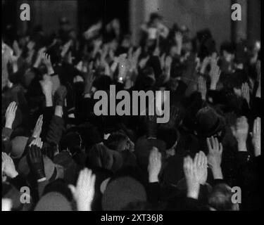 Adolf Hitler waving to crowds from his car at the head of a parade. The ...