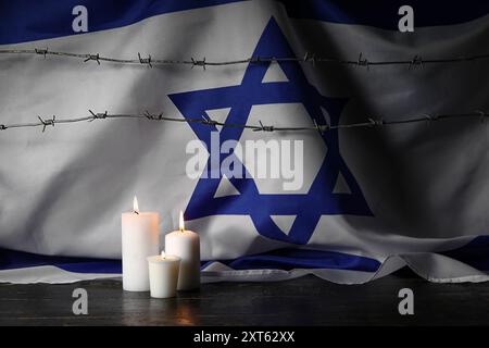 Burning candles with barbed wire and large flag of Israel on dark ...