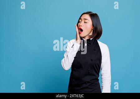 Sleepy asian waitress yawning and covering mouth with hand while ...