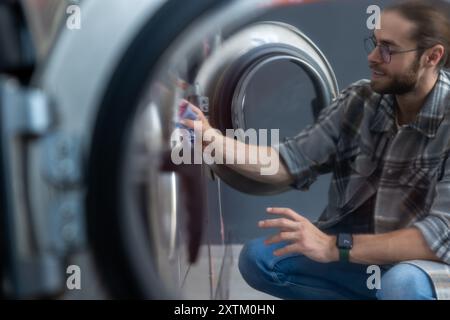 Hard working bearded man washing clothes at self-service laundromat ...