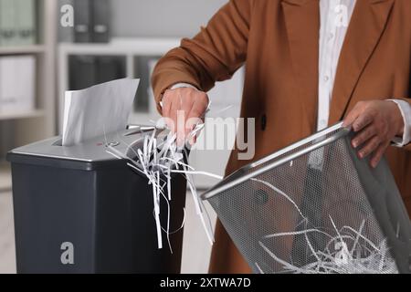Woman putting shredded paper strips into trash bin indoors, closeup ...