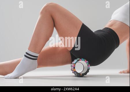 Faceless woman doing roller exercise for myofascial release on white ...