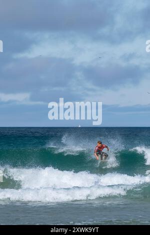 A surfer riding a wave at the iconic Fistral Beach in Newquay in ...