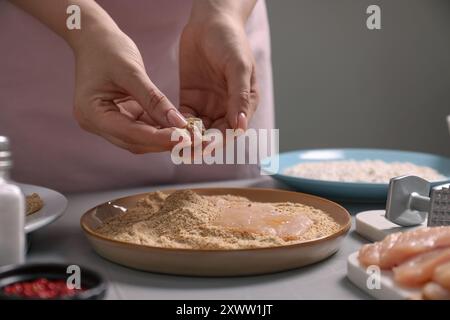 Making schnitzel. Woman coating slice of meat with bread crumbs at grey ...