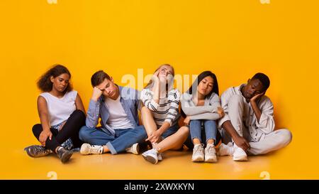 Bored classmates sitting over yellow background, being tired after ...