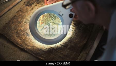 Senior archaeologist looks through magnifying lamp, studies ancient ...