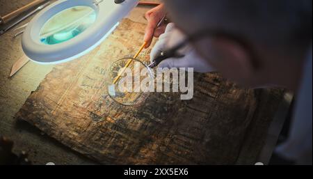 Senior archaeologist looks through magnifying lamp, studies ancient ...