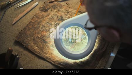 Senior archaeologist looks through magnifying lamp, studies ancient ...