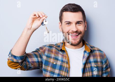 Happy house owner. Smiling young man holding keys and looking at camera ...