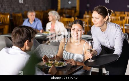 Waitress serves order of wine and wishes visitors young couple pleasant ...