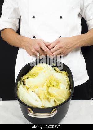 Chef in white jacket holding around a casserole of boiled cabbage Stock ...
