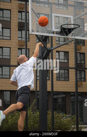 Sporty man tries to throw ball into basketball hoop on sports court at ...