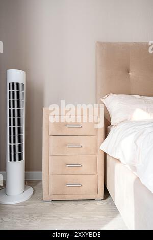White tower fan next to bedside table in light modern bedroom Stock ...
