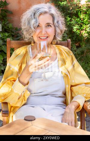 A woman wearing a yellow jacket and gray pants sits in a meditative ...