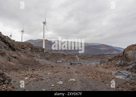 Several wind turbines stand in a harvested field with straw bales under ...